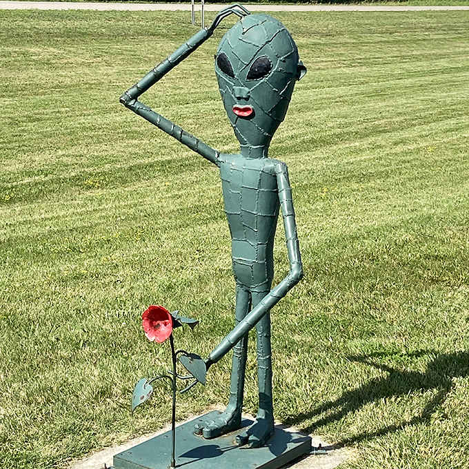 "Take me to your leader... or at least your best garden." This charming alien sculpture offers a flower, proving intergalactic visitors have good manners.
