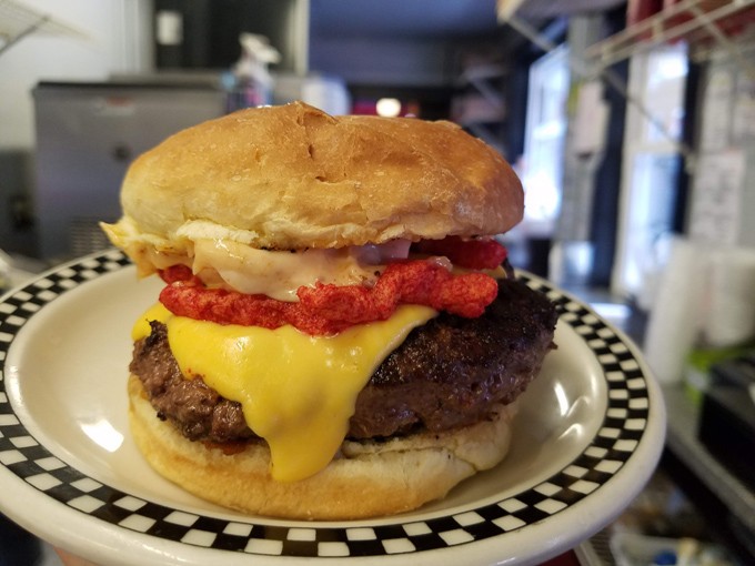 This isn't just any burger &ndash; it's a masterpiece of melty cheese and crispy toppings that requires both hands and possibly a bib.