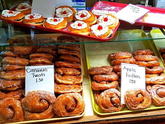 Fresh-baked cinnamon twists and apple fritters glisten under bakery lights, their golden surfaces promising buttery perfection with every bite.