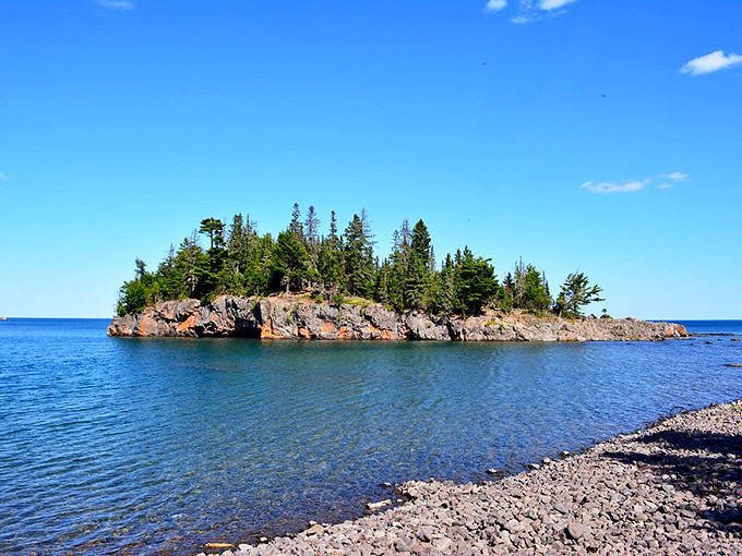 Lake Superior stretches endlessly from this rocky outcrop, its crystal waters shifting between deep blue and turquoise. The island stands sentinel in nature's magnificent theater.