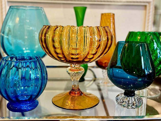 Vintage glassware catches the light like jewels, their amber, blue, and green hues creating an impromptu stained-glass effect when sunlight streams through.