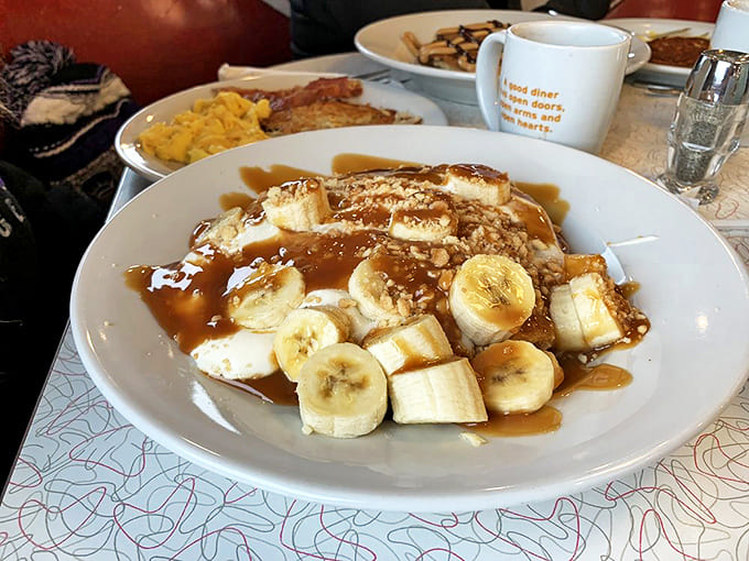 Banana cream pancakes that make breakfast feel like dessert – fresh slices nestled between fluffy layers, crowned with whipped cream and caramel drizzle.