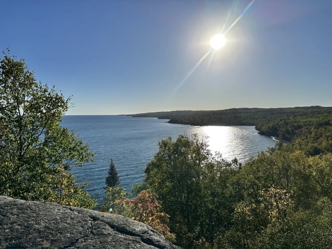 Sunlight dances across Lake Superior's vastness, painting the water with diamonds while forest-covered shores stand guard.