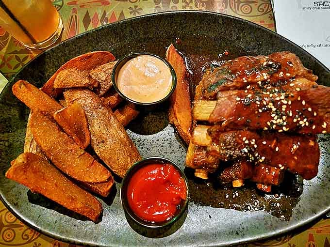 Huli Huli Ribs glisten with sweet-savory glaze alongside perfectly crisp sweet potato wedges—island comfort food that demands finger-licking appreciation.