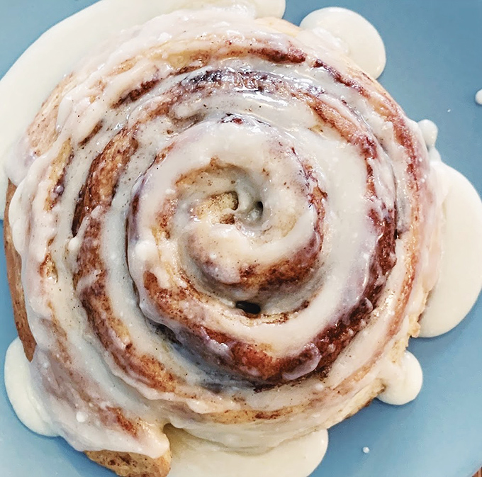A single cinnamon roll in all its glory &ndash; pillowy dough, generous cinnamon swirls, and cream cheese frosting that melts into every nook and cranny.