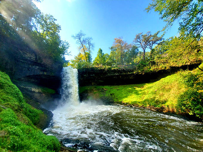 Sunbeams dance through the lush green canopy, perfectly spotlighting the falls as they plunge into the sparkling basin below.