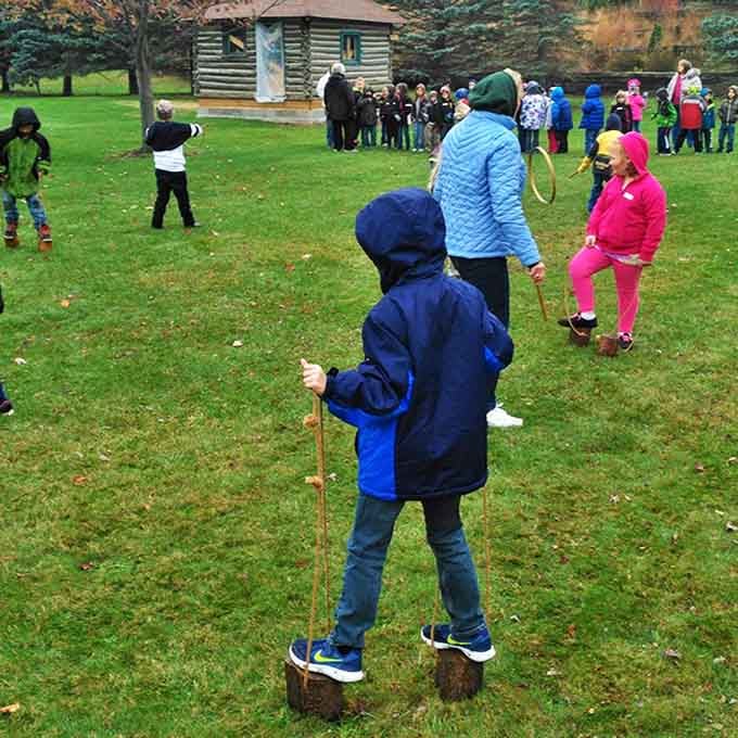 Children balance on wooden stilts outside a pioneer cabin, discovering that entertainment before electronics required actual balance!