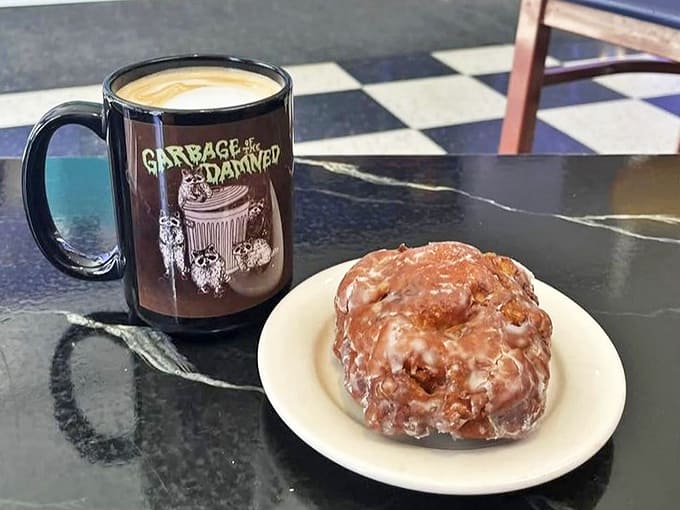 A perfectly glazed apple fritter pairs with coffee in a mug that reminds you garbage can indeed be divine&mdash;especially when it's this delicious.