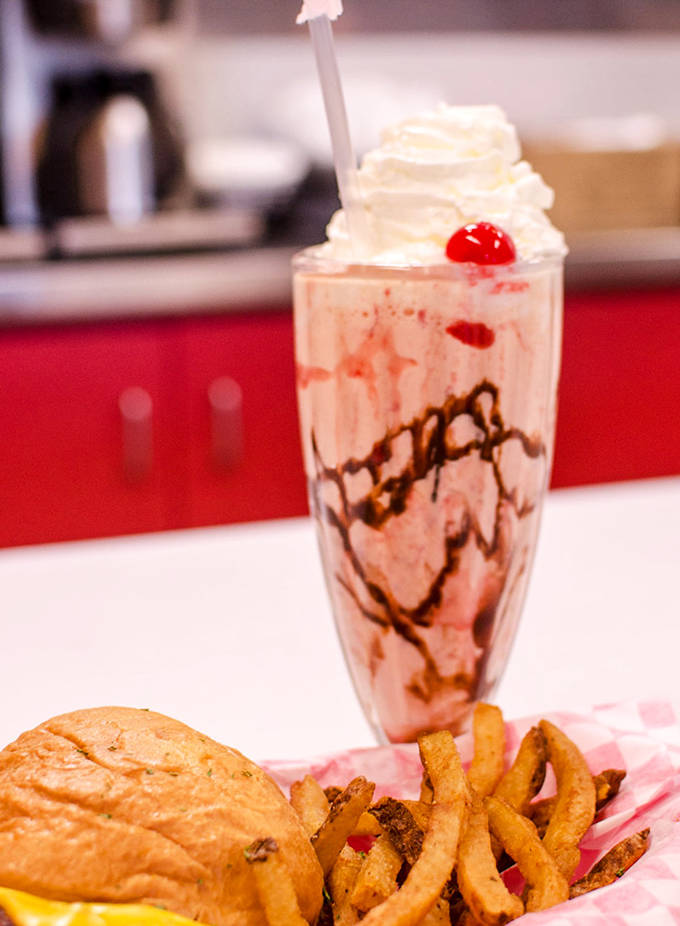 The strawberry milkshake arrives like a pink dream, accompanied by a burger that demands both hands and zero shame.