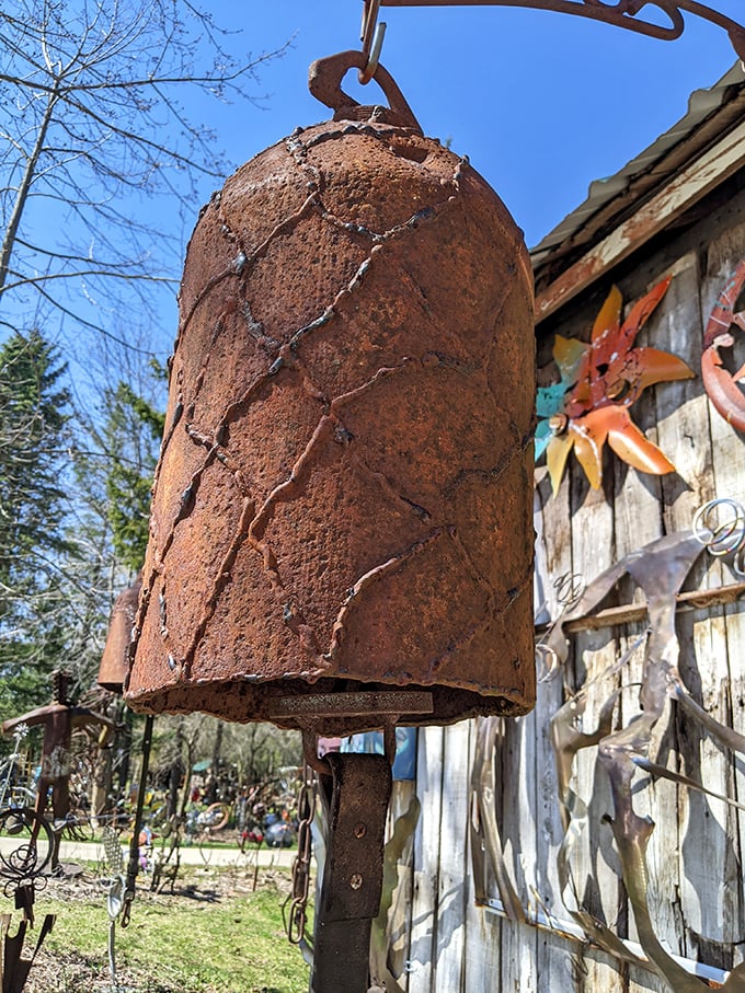 This rusted bell, once an industrial castoff, now hangs as a silent storyteller among weathered wooden walls and metal companions.