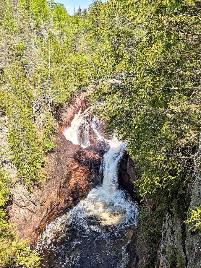 Framed by vibrant greenery, the waterfall's powerful cascade creates a hypnotic display as it vanishes into the earth's mysterious depths.