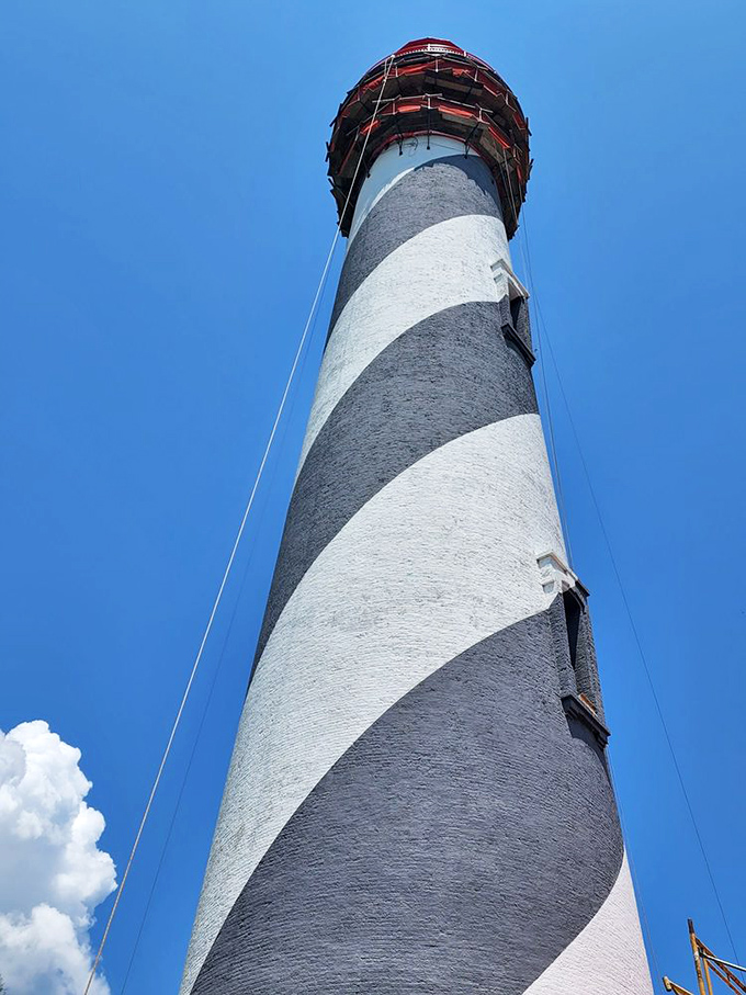 The lighthouse's bold stripes create dramatic shadows against the sky. From this angle, you can almost feel the structure's imposing presence.
