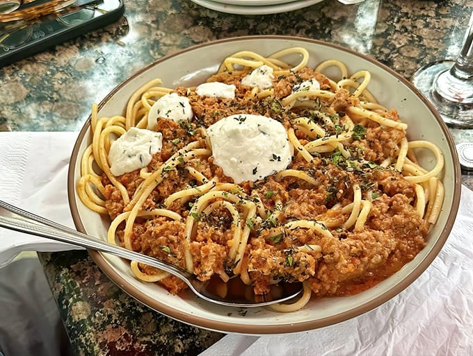 Spaghetti Bolognese arrives as a generous mountain of pasta crowned with dollops of creamy cheese, proving that Italian comfort food transcends all borders.