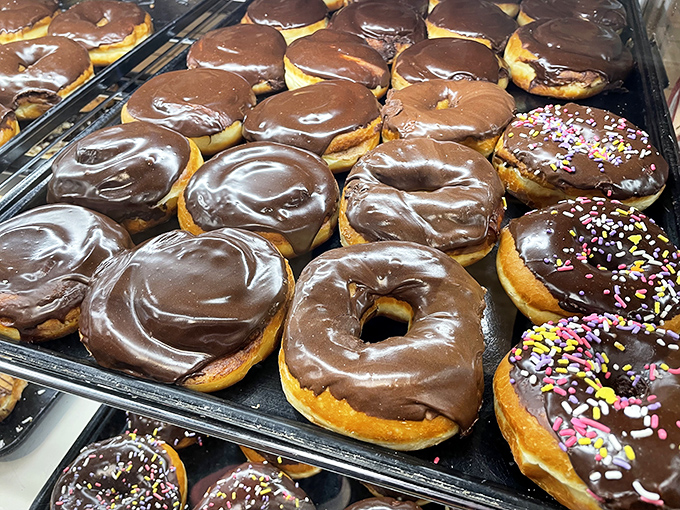 Chocolate-covered donuts glisten under the bakery lights, their glossy surfaces promising a richness that delivers with every bite.