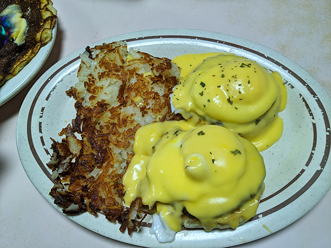 Eggs Benedict done right – hollandaise cascading over perfectly poached eggs alongside crispy hash browns that could convert a potato skeptic.