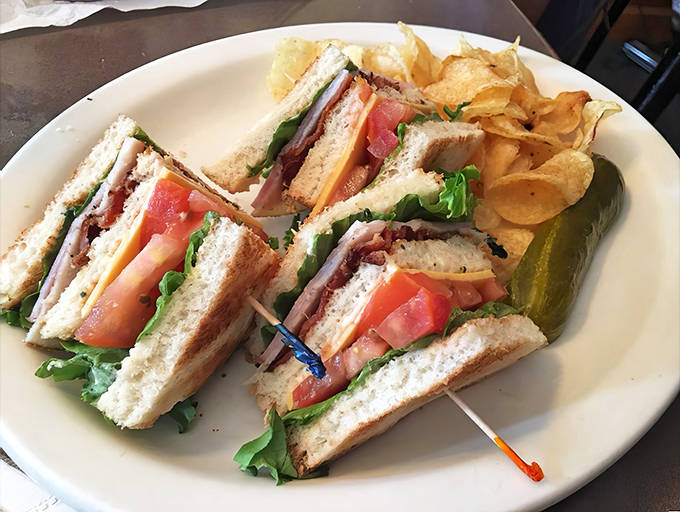 A club sandwich that requires both hands, strategic planning, and possibly an unhinged jaw&mdash;paired with house-made chips that crunch loud enough to turn heads.