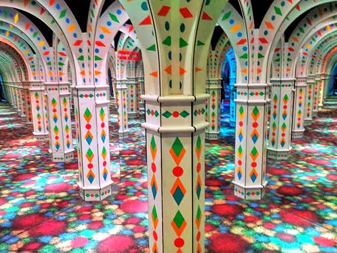 Geometric patterns and vibrant colors adorn each column, creating a festive atmosphere as visitors navigate the reflective labyrinth.