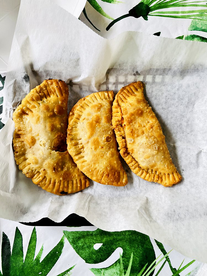 Golden-brown empanadas with perfectly crimped edges &ndash; little half-moon treasures that shatter delicately between your teeth, revealing savory secrets within.