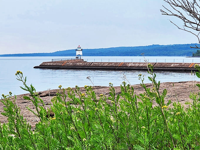 The lighthouse appears to float between sky and water when viewed from shore, a white exclamation point on Lake Superior's blue sentence.
