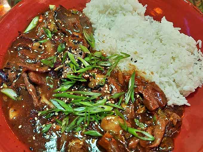 Tender slices of Bulgogi Beef swim in rich sauce alongside fluffy rice, garnished with vibrant green onions and sesame seeds.
