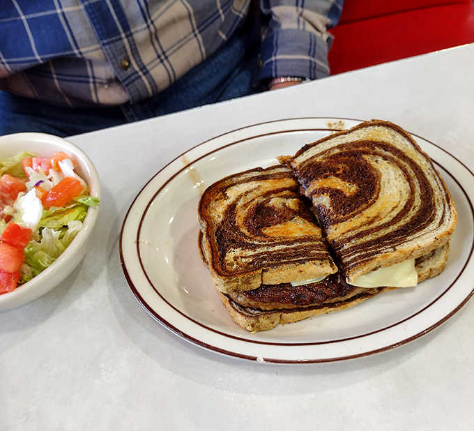 The patty melt sandwich arrives like edible artwork &ndash; grilled rye bread, melted cheese, and caramelized onions in perfect harmony.