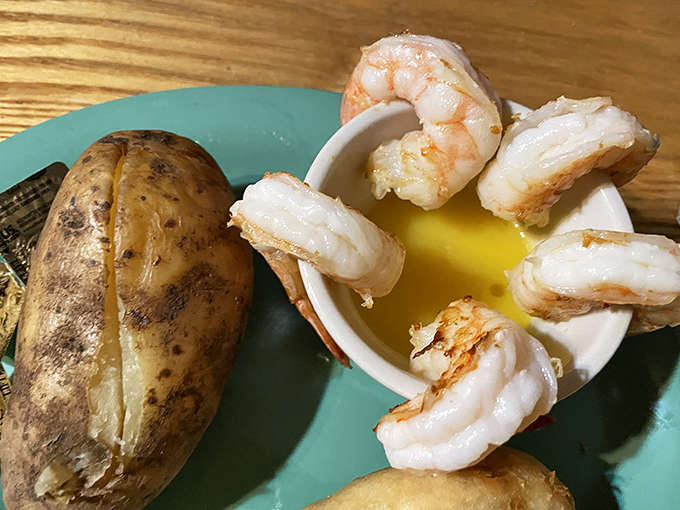 Plump, succulent shrimp arranged around a dish of melted butter, accompanied by a steaming baked potato &ndash; simple pleasures done right.