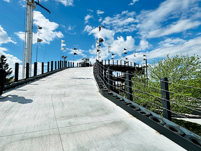 Flags flutter in the Michigan breeze as the track climbs skyward, marking the path where courage meets concrete in a dance of speed.