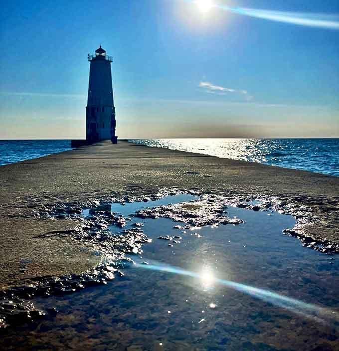 Daytime: A sailboat glides past the lighthouse, creating the kind of scene that makes amateur photographers look suspiciously professional.