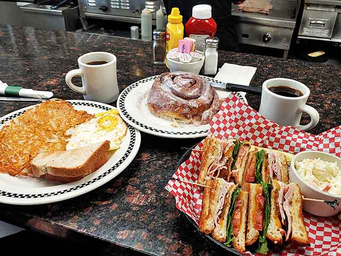 The breakfast trifecta: golden hash browns, a club sandwich that requires structural engineering, and that famous cinnamon roll centerpiece.