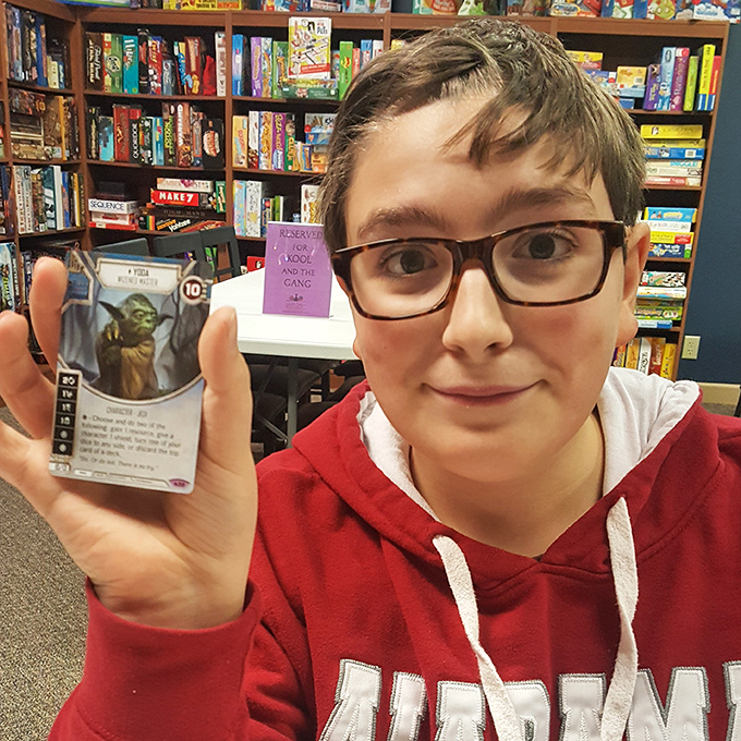 A young enthusiast proudly displays a prized Yoda card, the joy of collecting crossing generational boundaries in this gaming sanctuary.