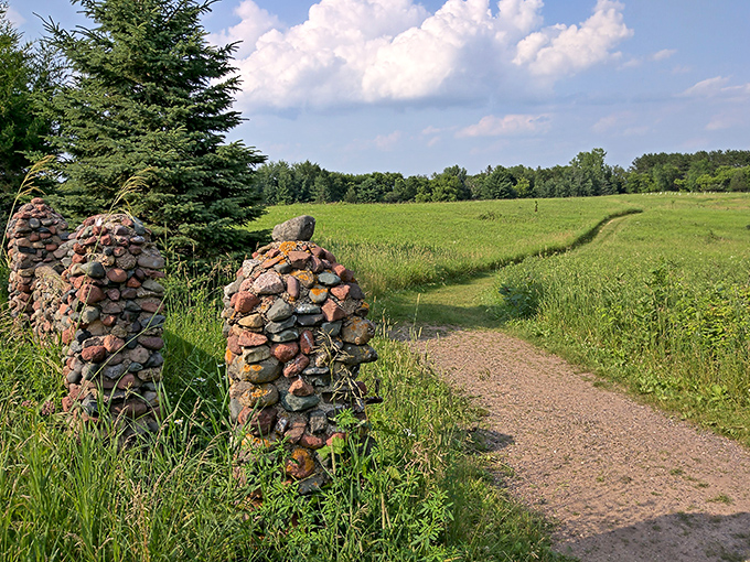 Stone pillars stand like ancient sentinels, marking the entrance to trails that wind through meadows of dancing prairie grasses.