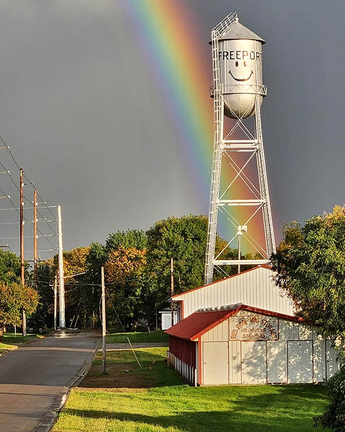 Nature adds its own magic as a perfect rainbow arcs behind the smiling water tower, creating a postcard-worthy moment of small-town charm.