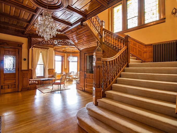 Inside, a grand staircase with intricate woodwork welcomes guests to spaces that blend historic elegance with modern comfort.