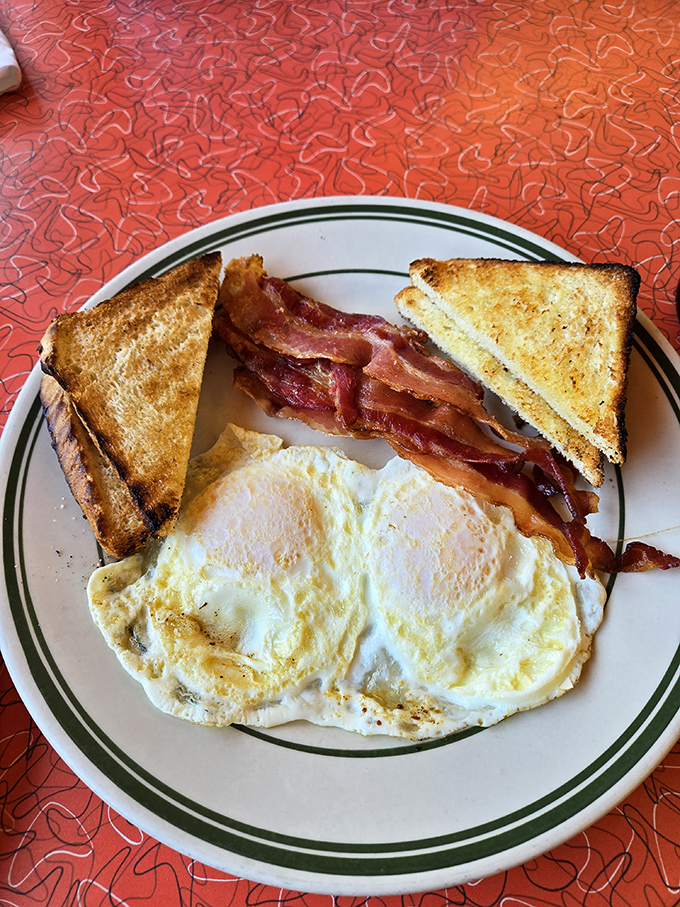 The classic breakfast trinity: eggs sunny-side up, bacon with that ideal crisp-yet-chewy texture, and toast ready for dipping into golden yolks.