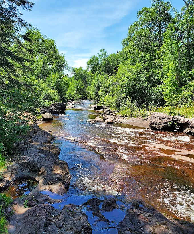 The Caribou River meanders peacefully between rocky shores, a gentle prelude to its dramatic plunge downstream.