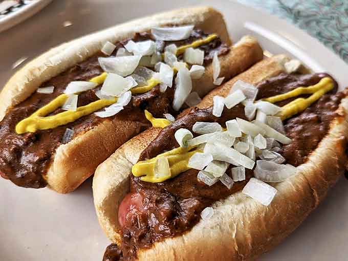 Two perfectly grilled hot dogs nestled in soft buns, smothered in homestyle chili and topped with diced onions and mustard's yellow zigzag signature.