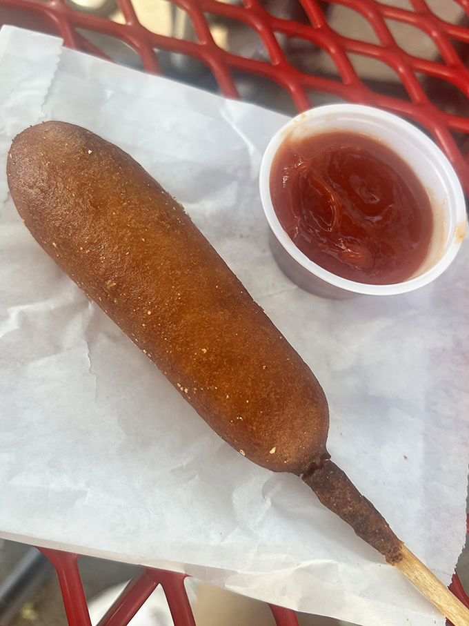A perfectly golden corn dog awaits its fate, accompanied by a side of tangy ketchup for the ultimate nostalgic bite.