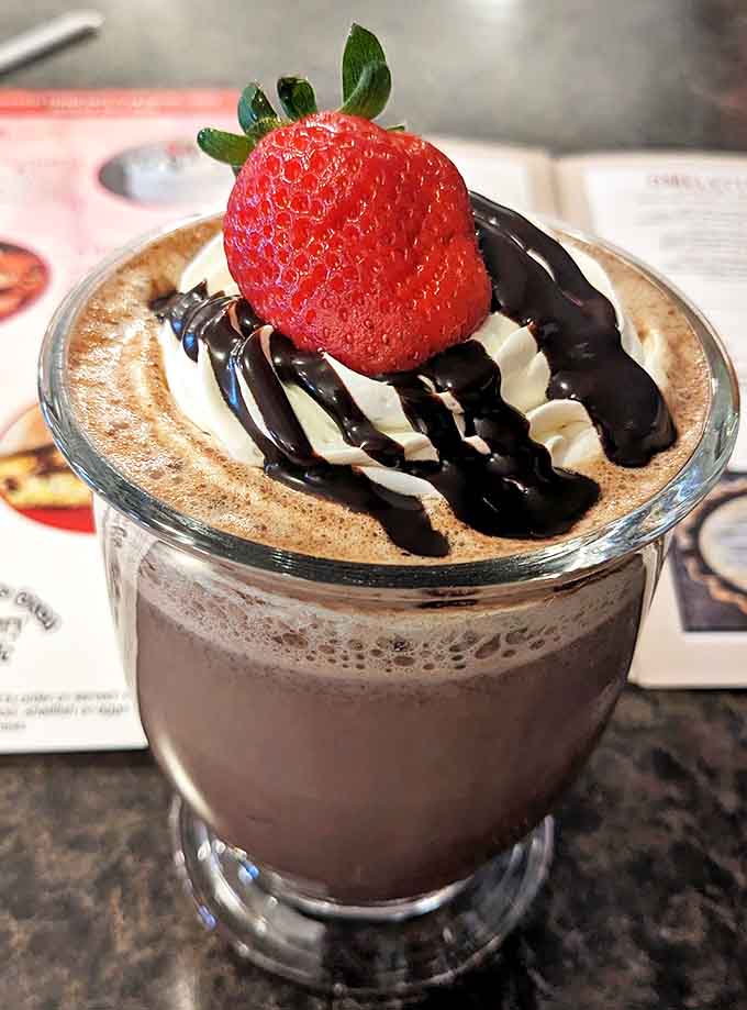 Hot chocolate elevated to an art form &ndash; topped with real whipped cream, chocolate drizzle, and a fresh strawberry in a proper glass mug.