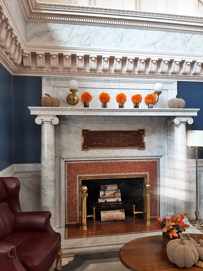 The marble fireplace stands as the heart of the reading room, its elegant mantel adorned with seasonal touches that bring warmth to this temple of learning.