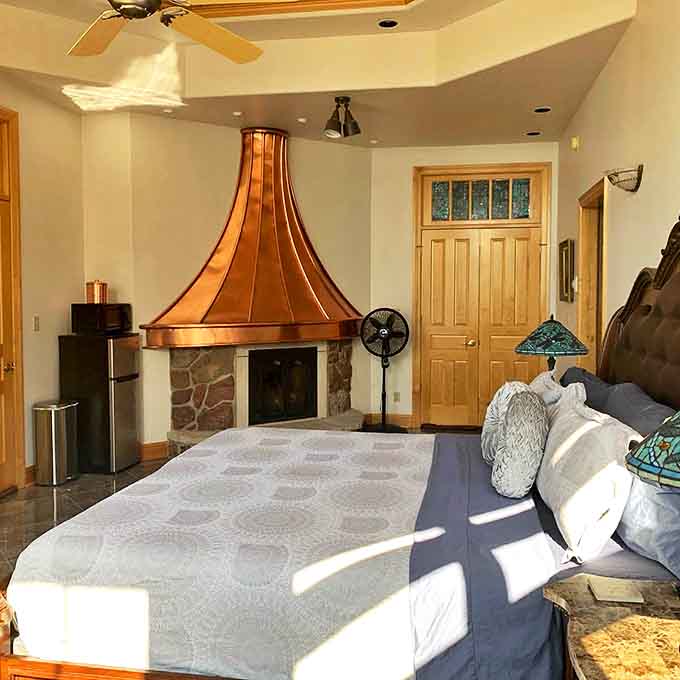 Copper accents crown this bedroom's fireplace, where the dancing flames create the perfect ambiance for romance or quiet contemplation.