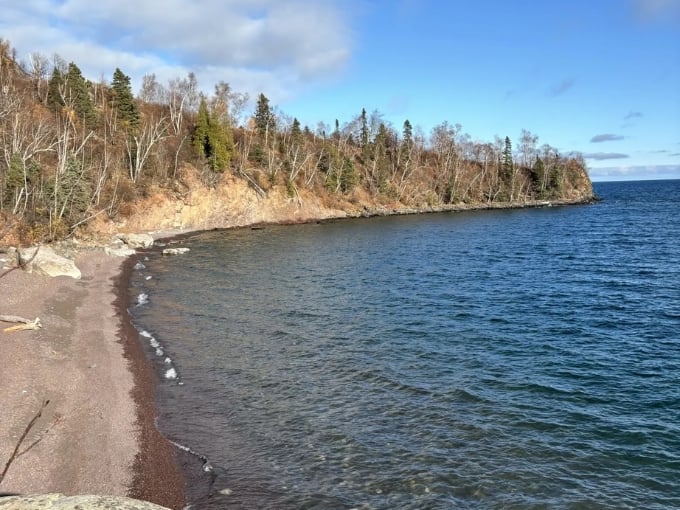 Autumn shoreline curves gently into distance, where forest meets water in that perfect Minnesota harmony we all crave.