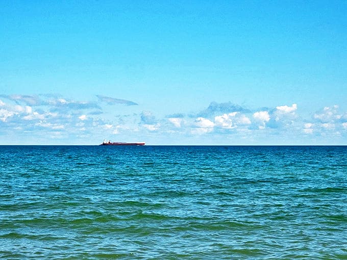 Endless blue horizons meet ancient stones &ndash; a passing freighter reminds visitors of Lake Huron's dual role as natural wonder and working waterway.