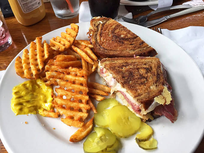 The Reuben sandwich arrives piled high with corned beef and sauerkraut, accompanied by perfectly seasoned waffle fries and crisp pickle spears.