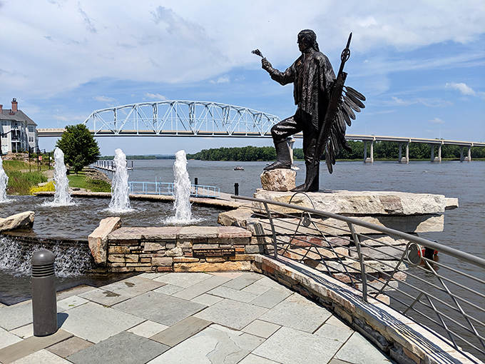 A bronze Native American figure stands proudly overlooking the Mississippi, where dancing fountains and river views create a contemplative riverside retreat.