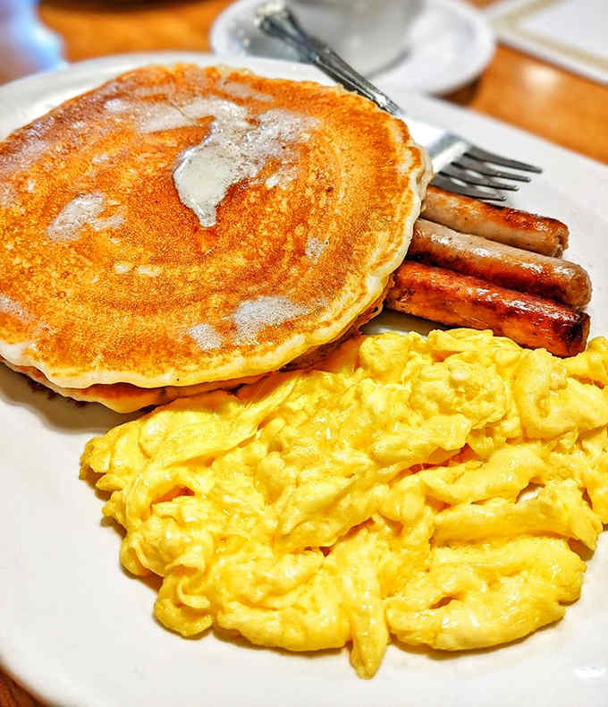 The breakfast trifecta: golden pancakes, perfectly scrambled eggs, and sausage links that snap with each bite.