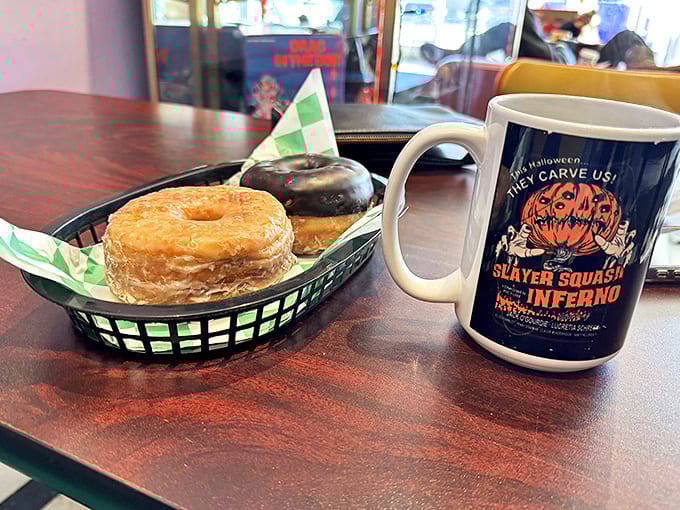 Golden donuts nestled in a basket beside Halloween-themed coffee&mdash;because nothing says "good morning" like sugar and spooky vibes.