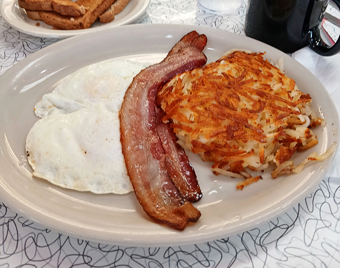 The holy trinity of breakfast perfection: eggs with edges just crispy enough, bacon with the ideal bend, and hash browns worth fighting over.