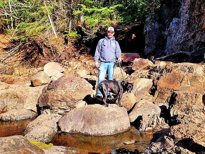 A visitor and his canine companion explore the rocky terrain near the falls, demonstrating the accessible adventure awaiting park guests.