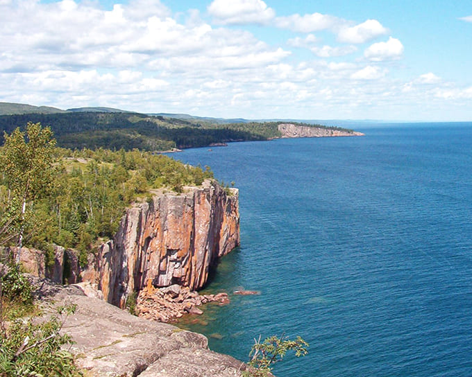Basalt cliffs glow orange in evening light, standing sentinel over the vast blue expanse of America's greatest lake.