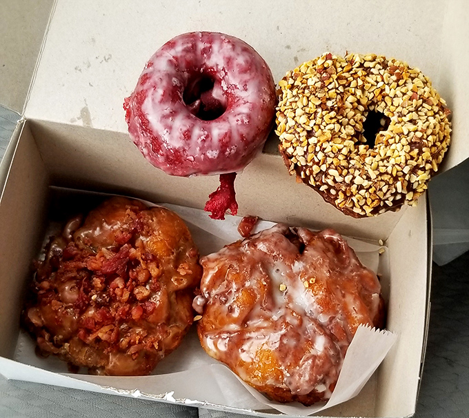 This donut quartet showcases the shop's range: a vibrant red velvet, chocolate with nuts, and two variations of their legendary apple fritters.